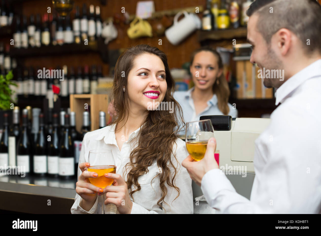Smiling bartender and young guests couple with wine at bar counter ...