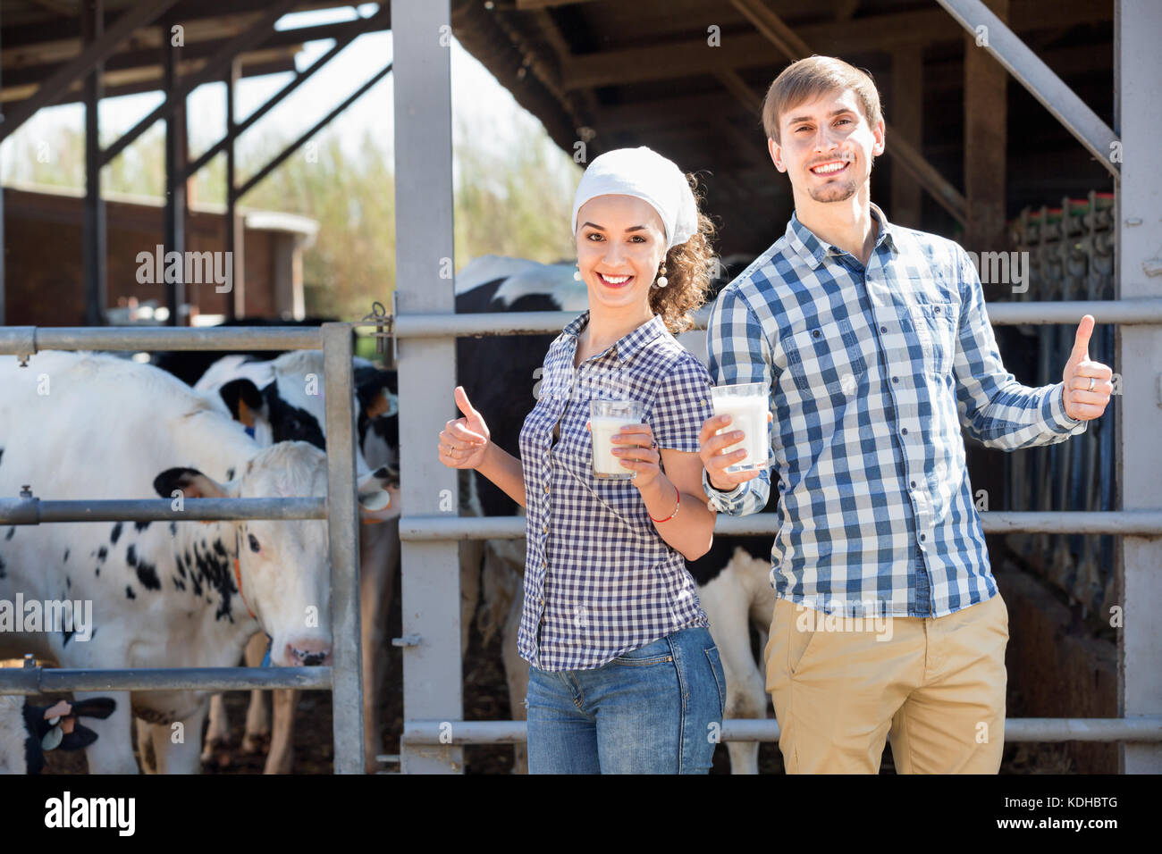 Portrait of two smiling farm workers holding glass with milk close to ...