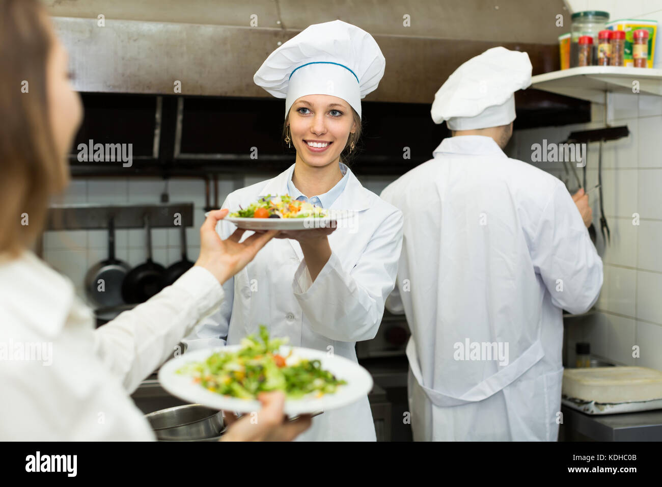 Waitress taking dish from smiling chef on cafe kitchen. Selective focus ...