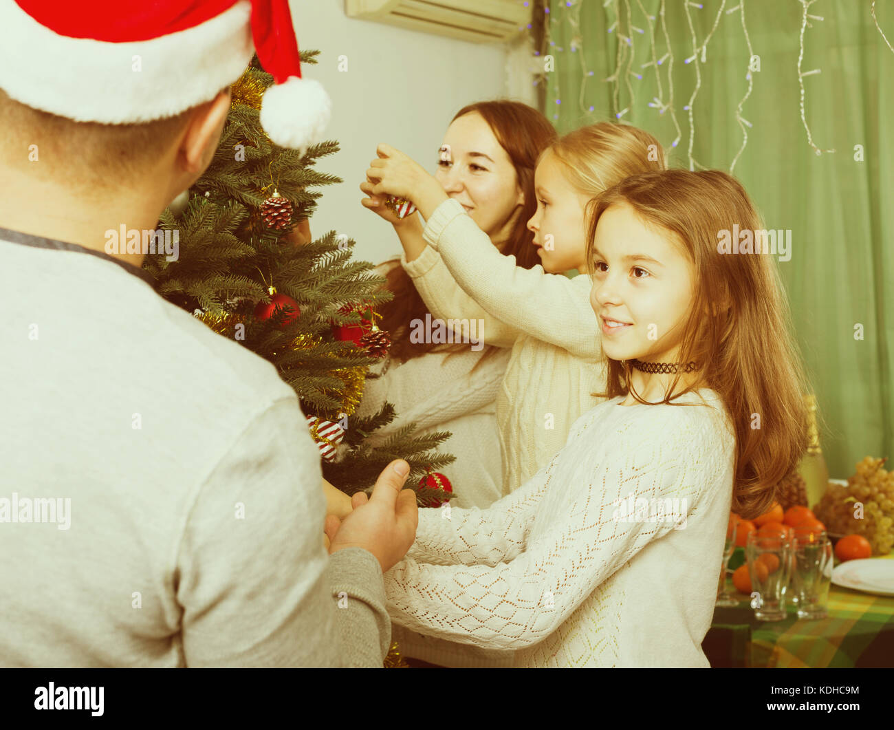 Four happy people decorating Christmas tree at home Stock Photo - Alamy