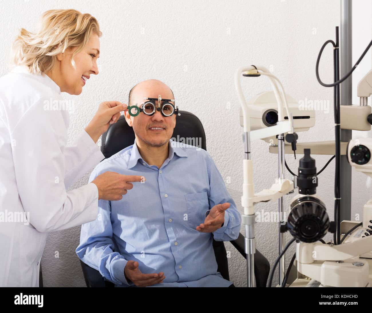Positive senior woman optician doing eye check up to elderly smiling ...