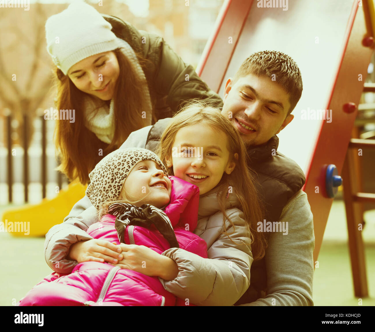 smiling spanish parents with two daughters playing at children's slide ...