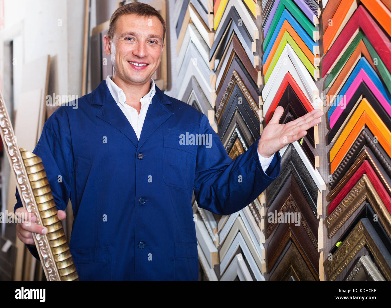 Cheerful man worker holding picture frame details on counter in studio ...