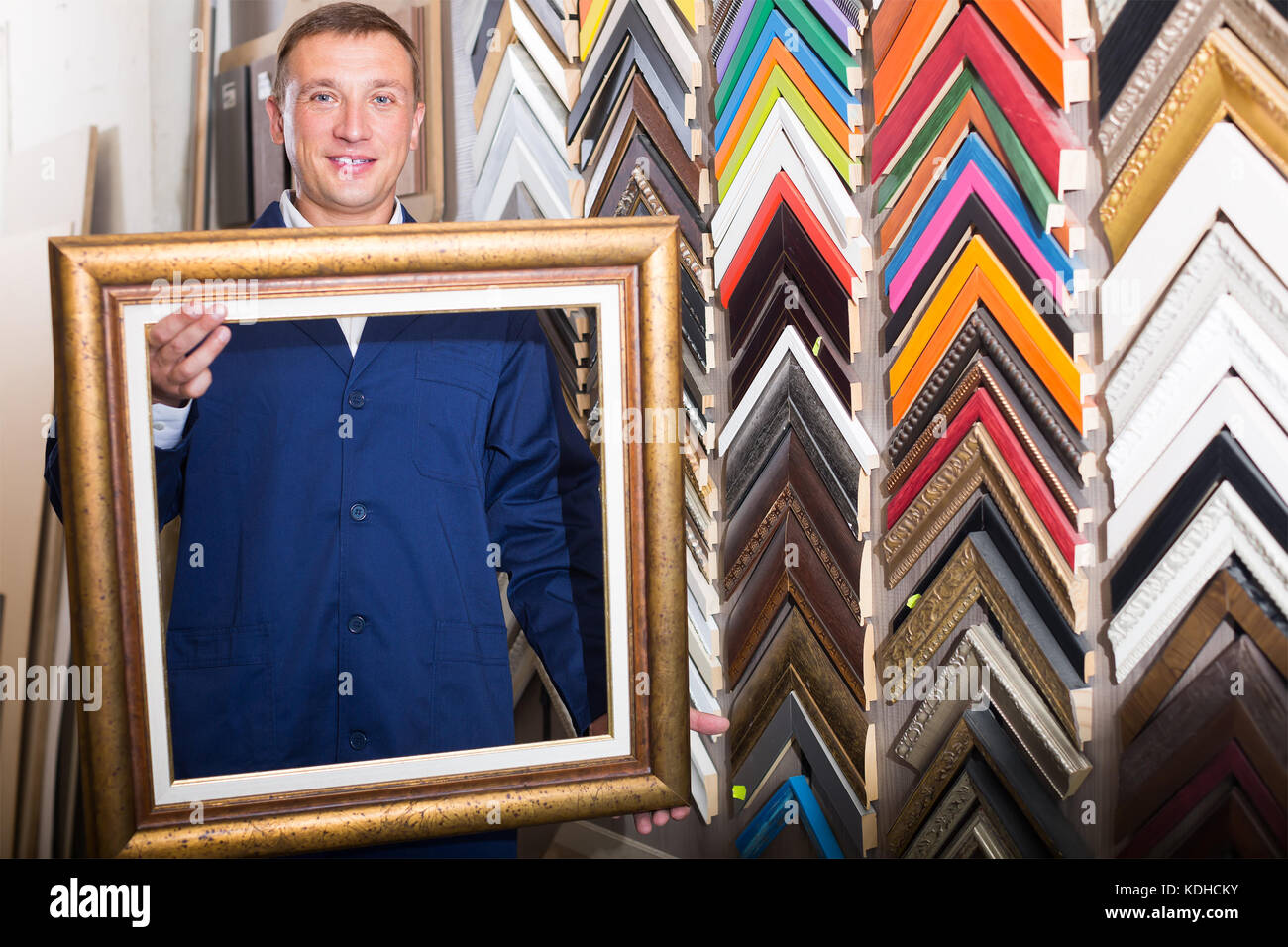 Cheerful workman holding wooden picture framing moulding in atelier ...