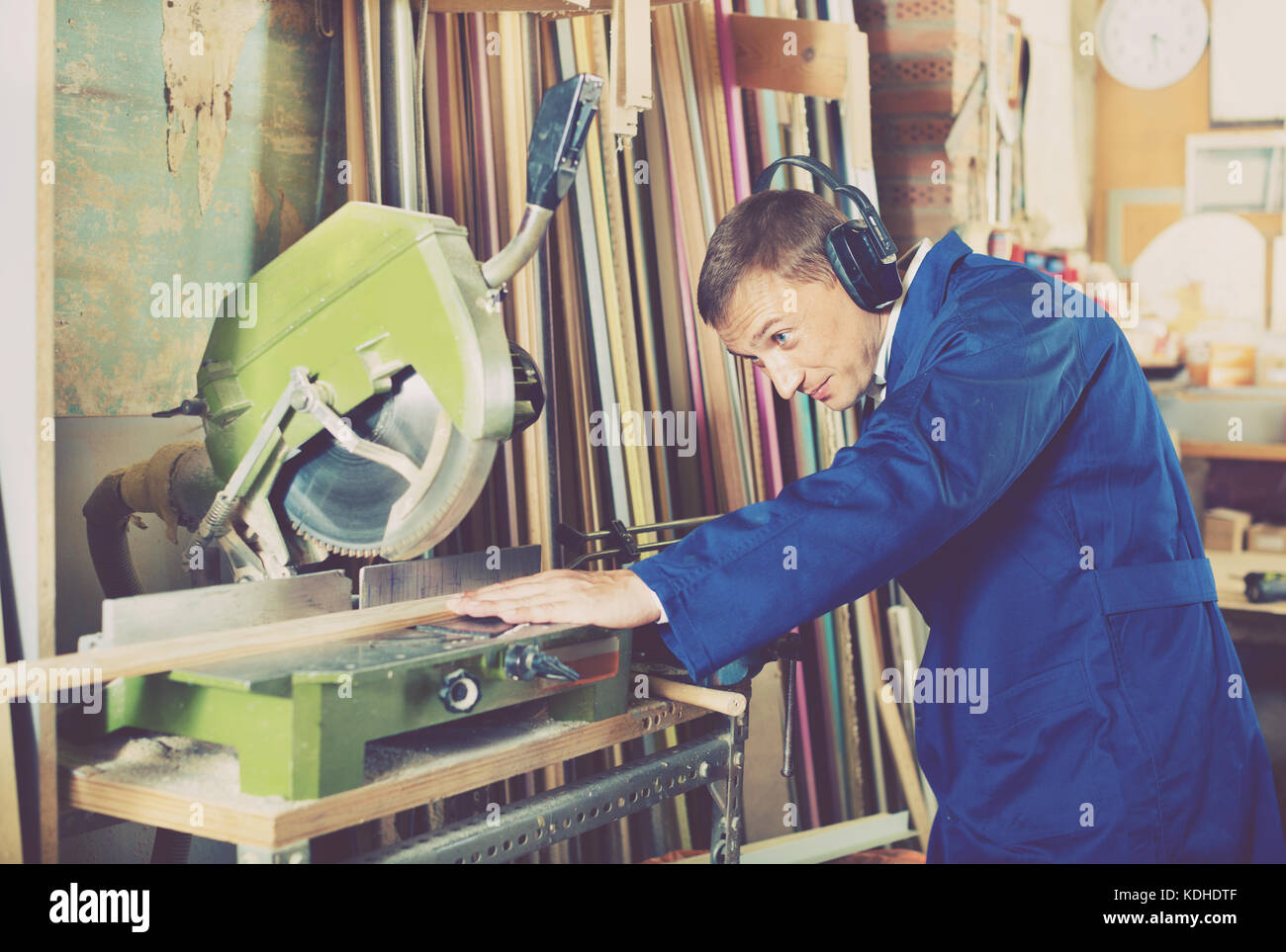 Smiling glad man wearing protective workwear operating circular saw in ...