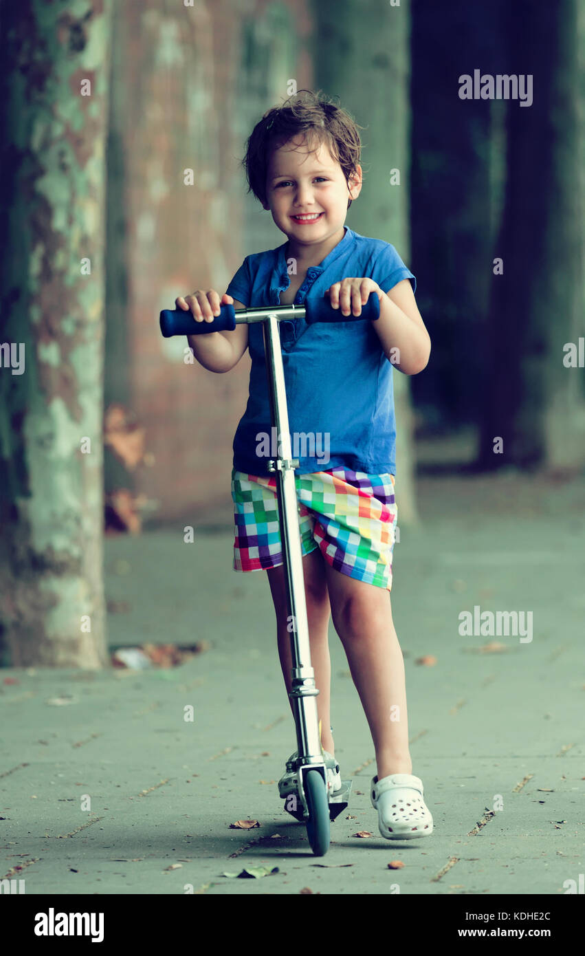 Smiling positive happy little girl riding on scooter in park Stock ...
