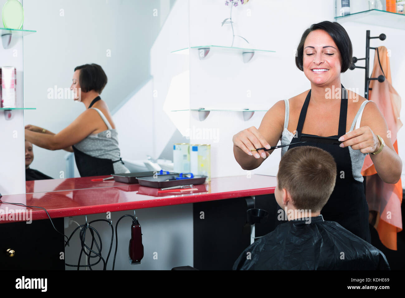 Smiling female professional hairdresser cutting boy in elementary ...