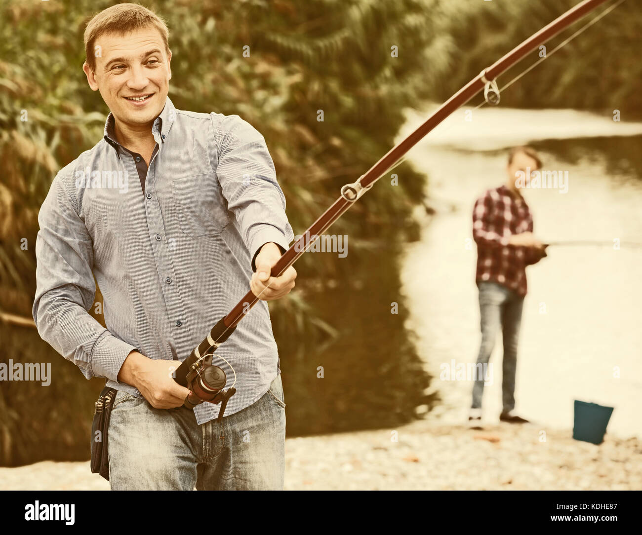 Positive adult man fishing using a rod from water side on lake Stock ...