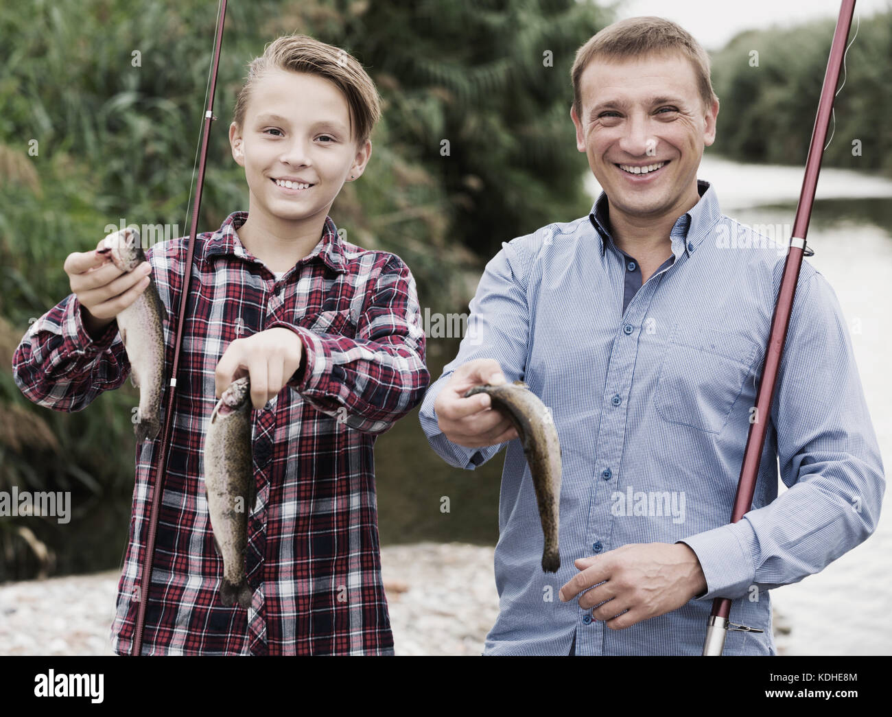 Glad man with teenager boy standing together and showing catch fish ...