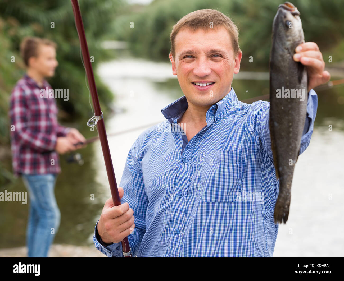Positive fisherman holding catch freshwater fish in hands Stock Photo ...