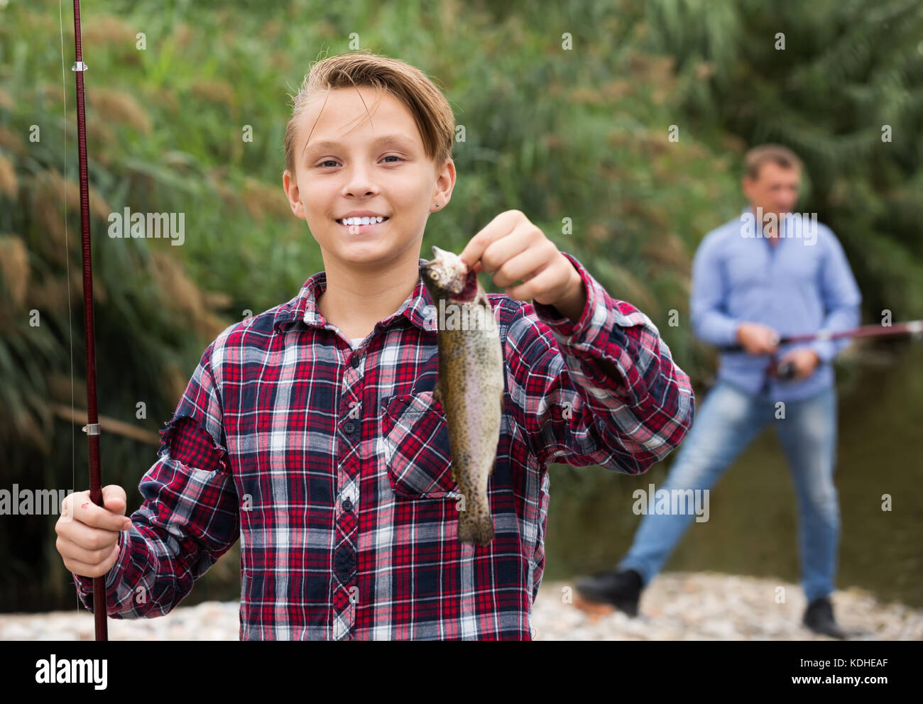 Smiling teenage boy holding catch freshwater fish in hands on vacation ...