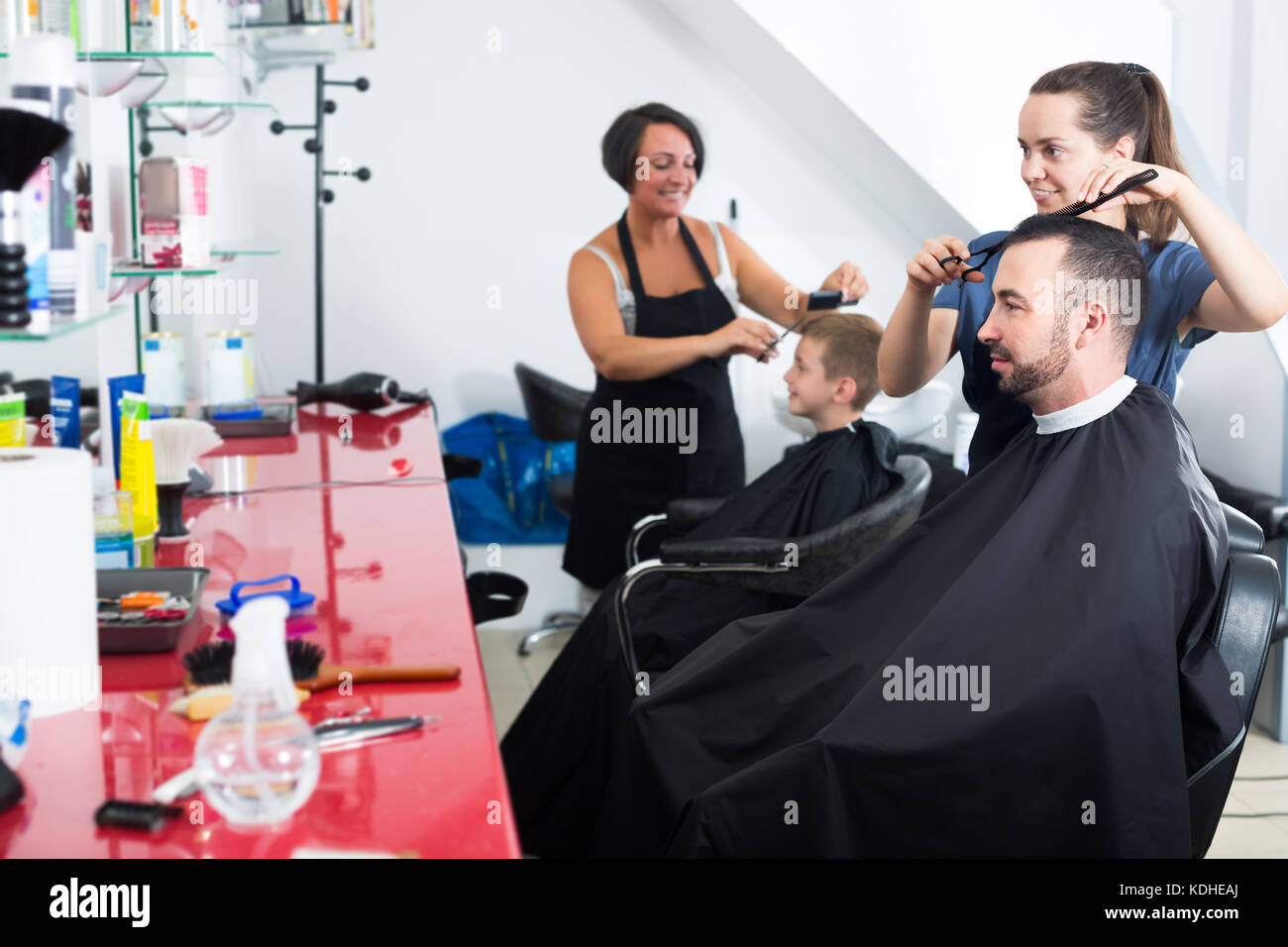 Glad woman hairdresser cutting male client in crowded beauty salon ...
