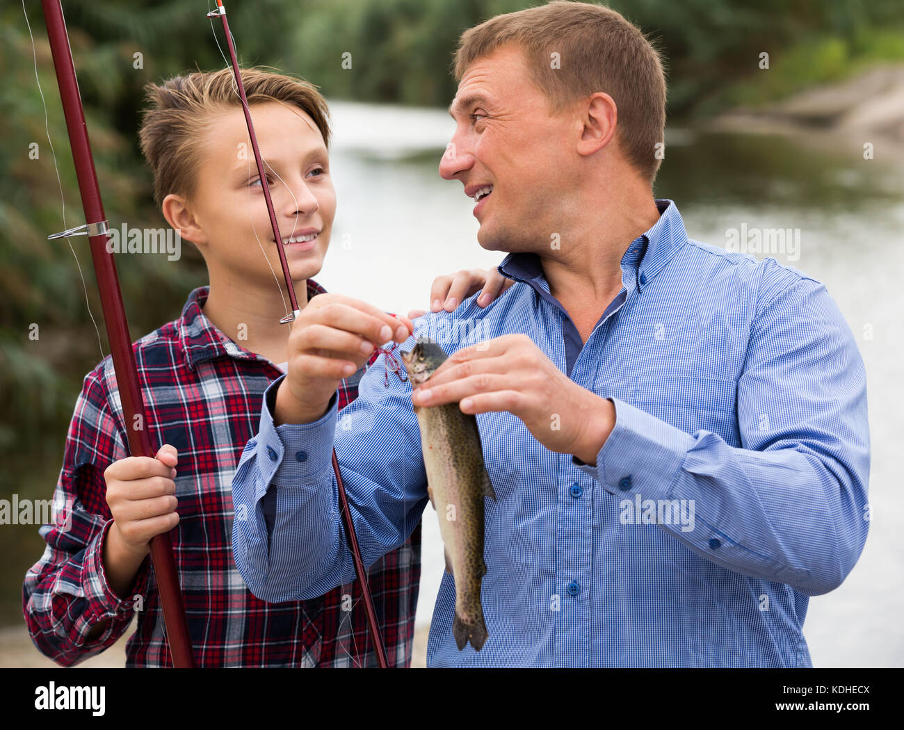 Portrait of adult man with teenager son looking at fish on hook in ...