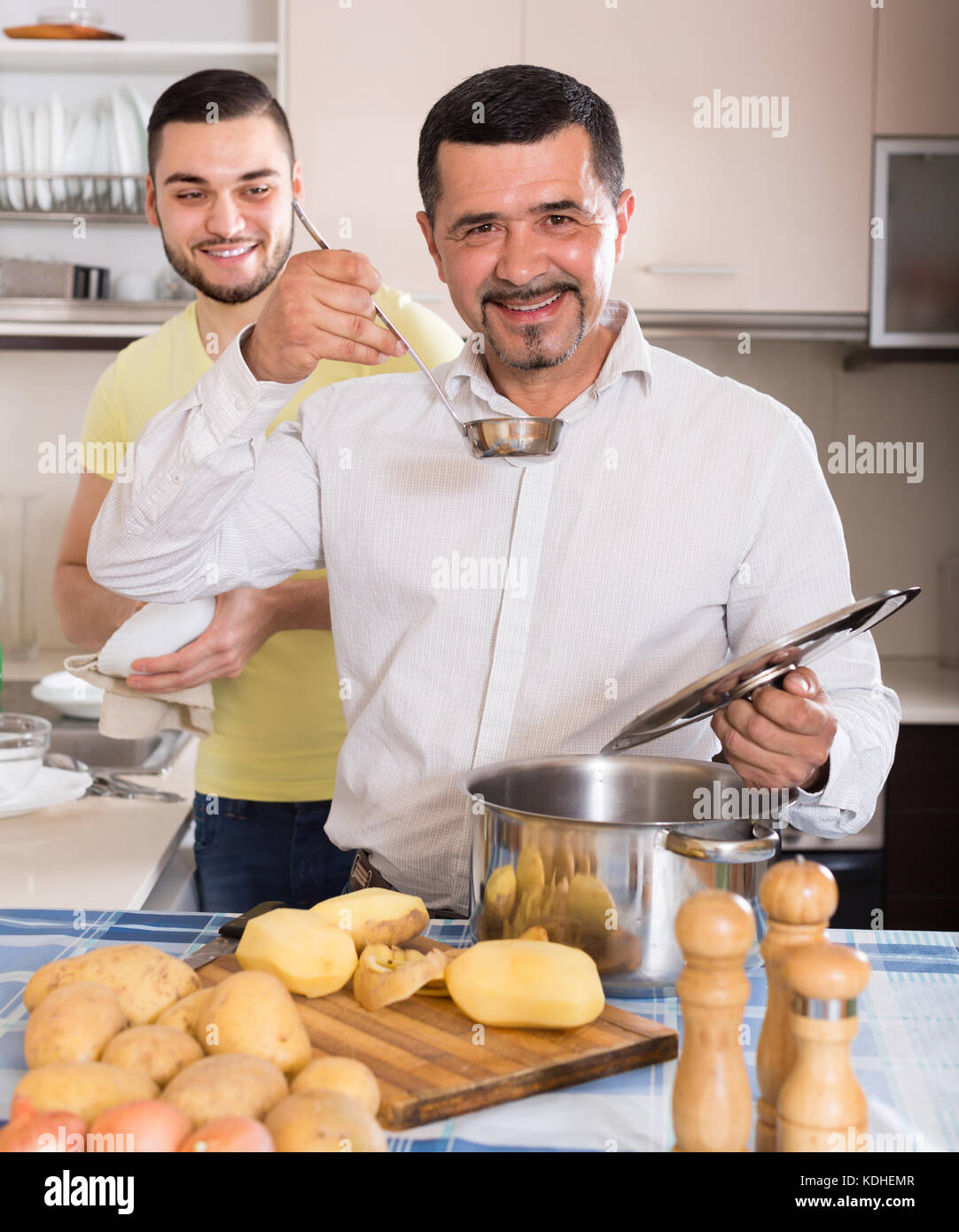 Two smiling male friends cooking potato soup and doing dishes at ...
