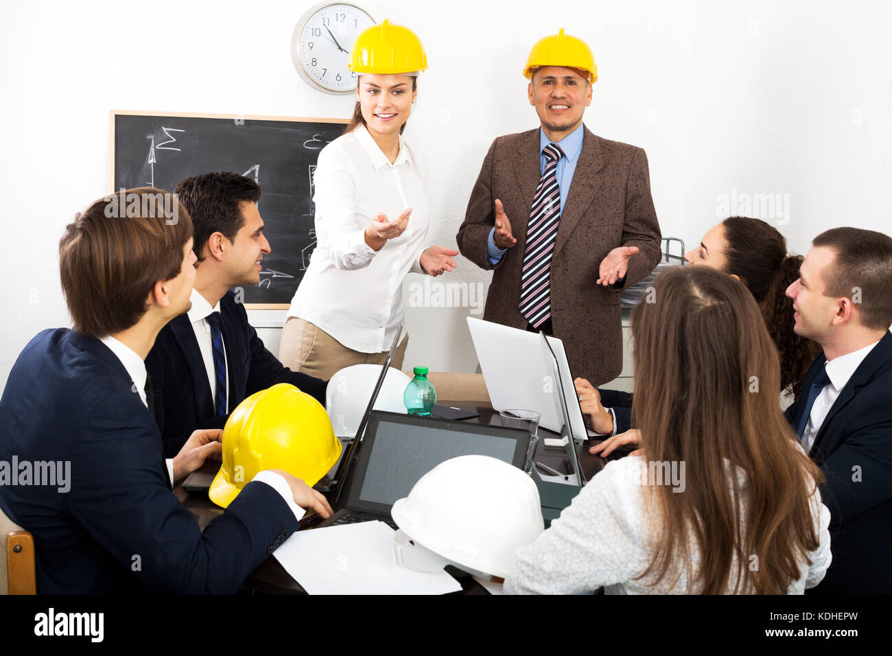 Positive professionals with laptops and helmets having presentation of ...