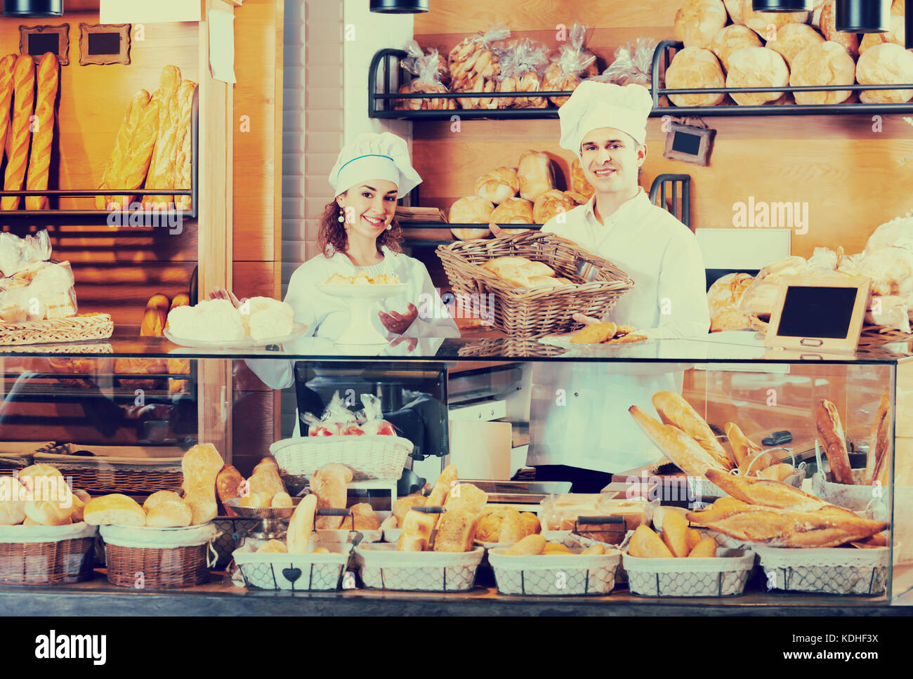 Smiling man and girl selling fresh pastry and loaves in bread section ...