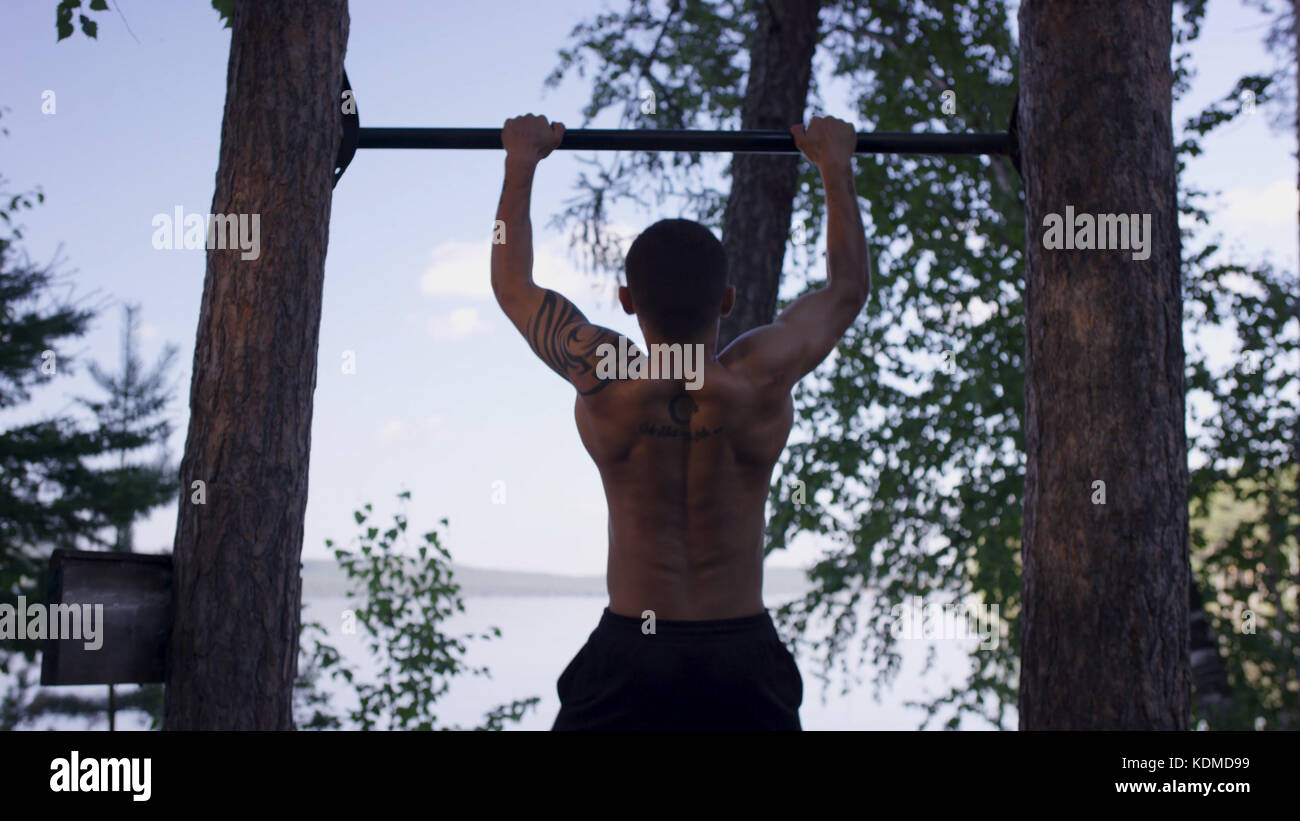 Back view of tattooed man doing pull-ups while having workout in ...
