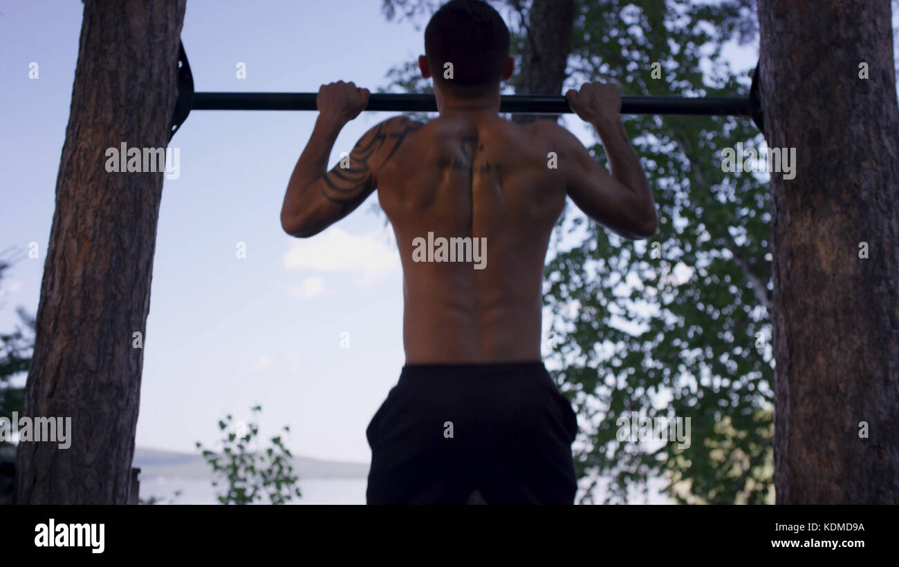 Back view of tattooed man doing pull-ups while having workout in ...