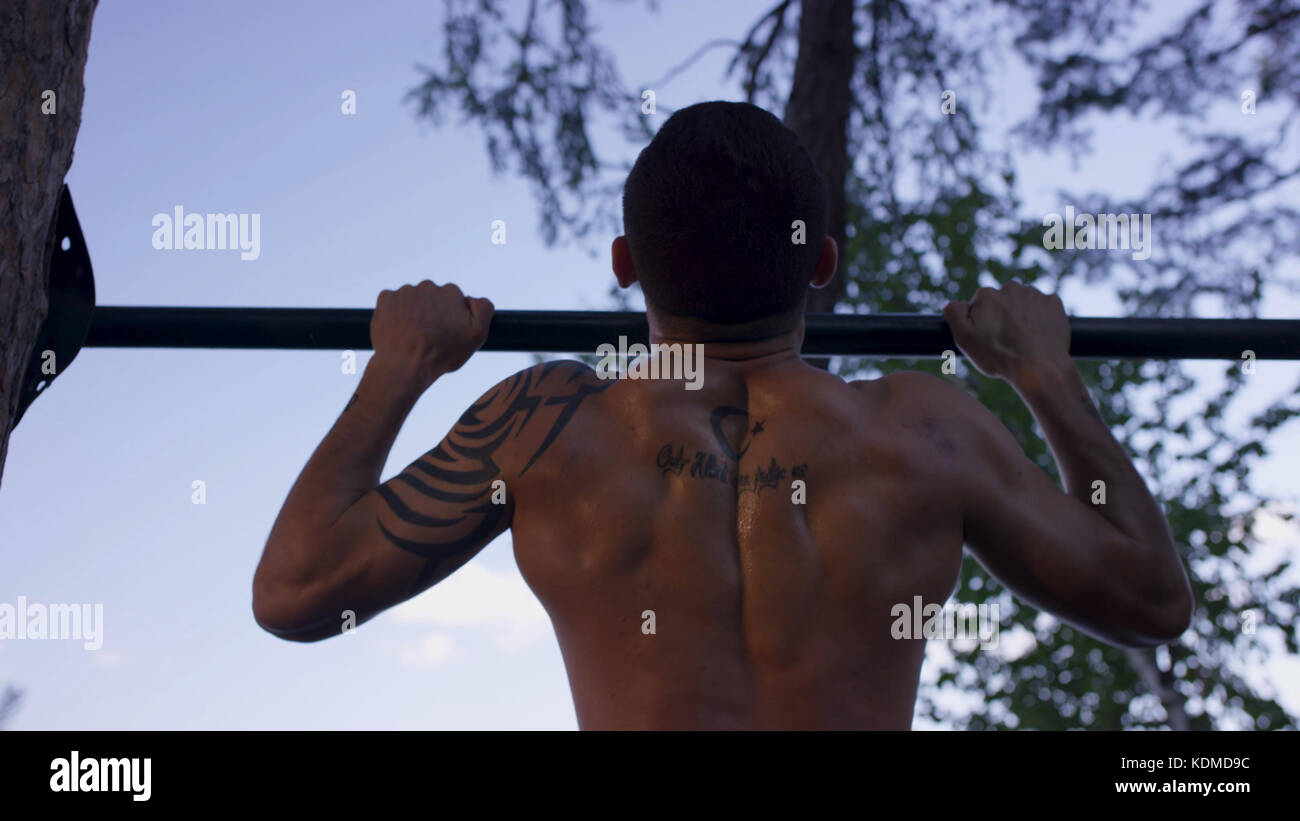 Back view of tattooed man doing pull-ups while having workout in ...
