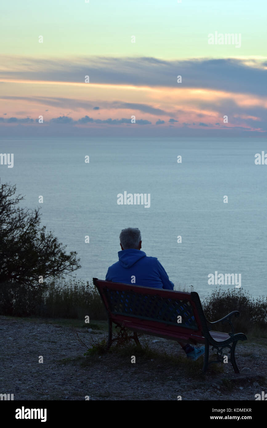 a man sitting on a bench at sunset looking out to sea and thinking ...