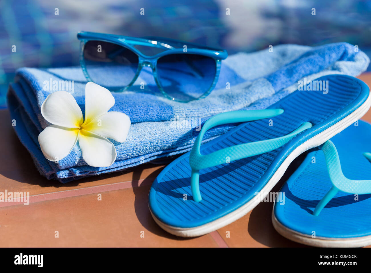 Blue slippers, sunglasses and towel on border of a swimming pool ...
