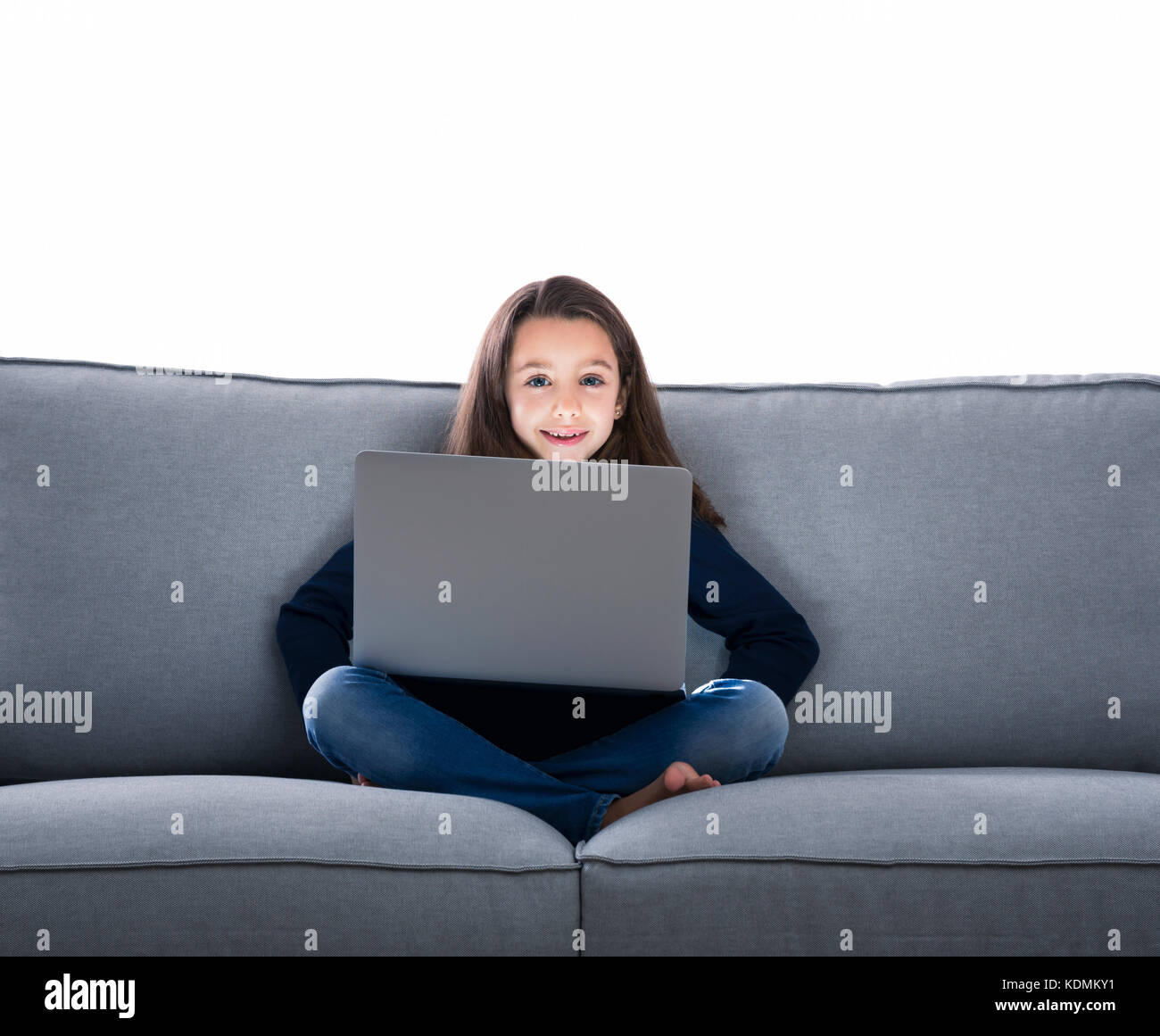 Happy little girl sitting on a couch and working a laptop Stock Photo ...