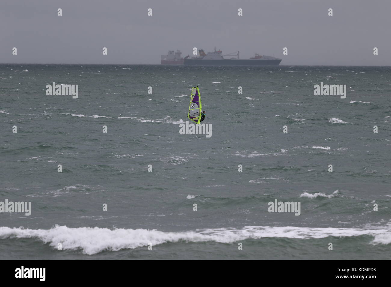 A windsurfer in rough seas off Sandown, Isle of Wight, with a big ship ...