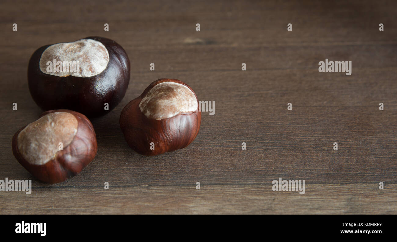 three wild chestnuts on a wooden table Stock Photo - Alamy