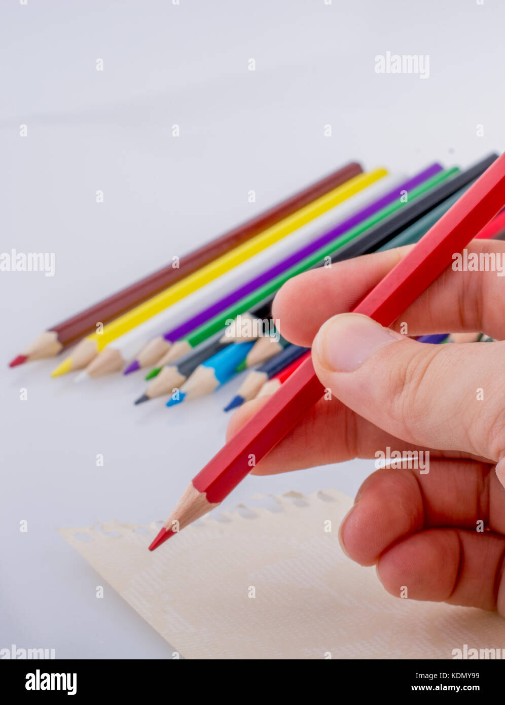 Hand holding a pencil beside the colorful pencils on a white background ...