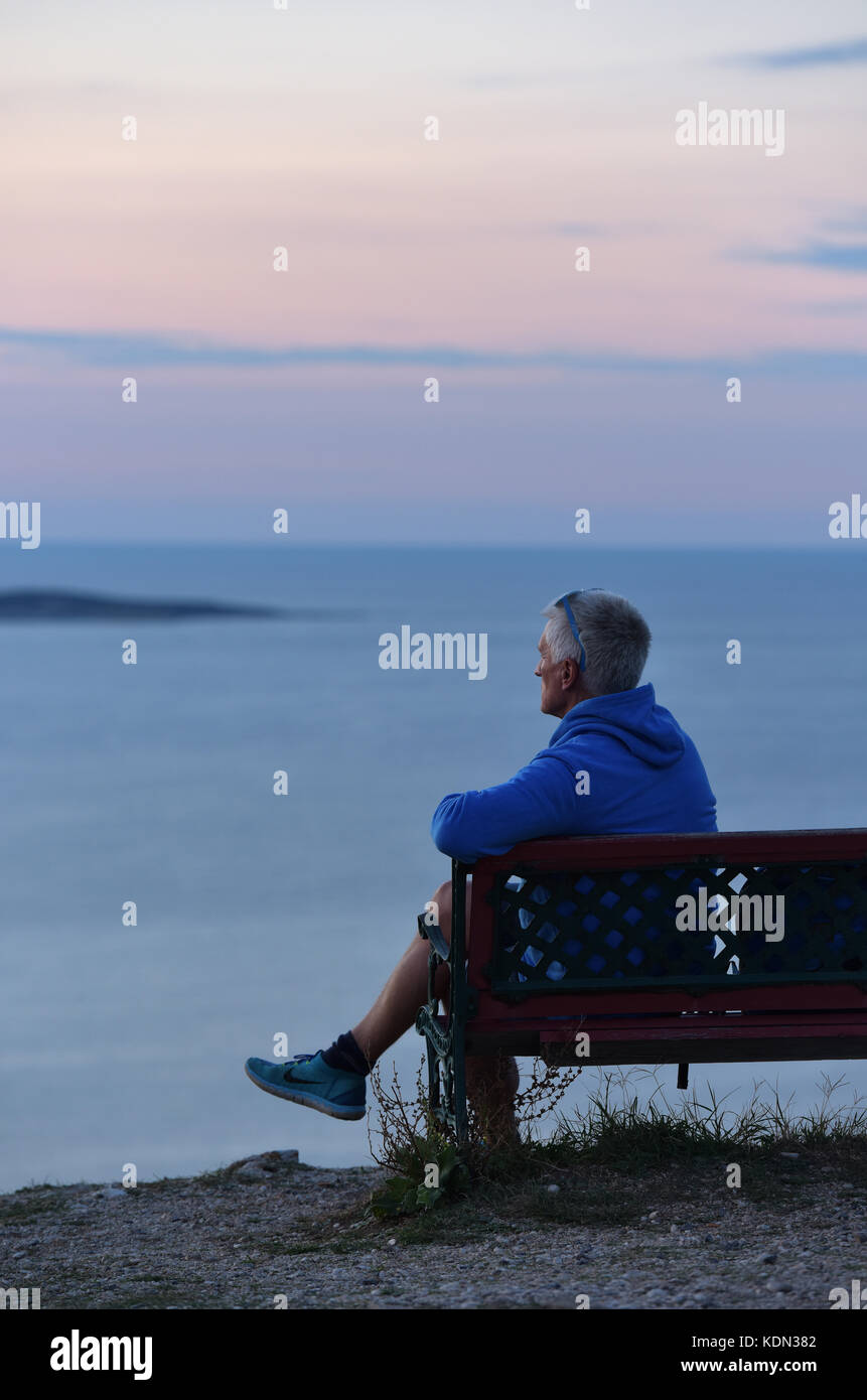 a man sitting on a bench watching the sunset or sun go down over the ...