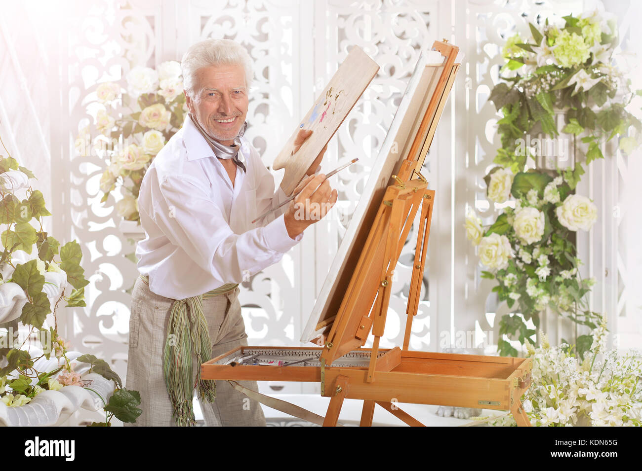 Senior man drawing picture on drawing easel in light room Stock Photo ...