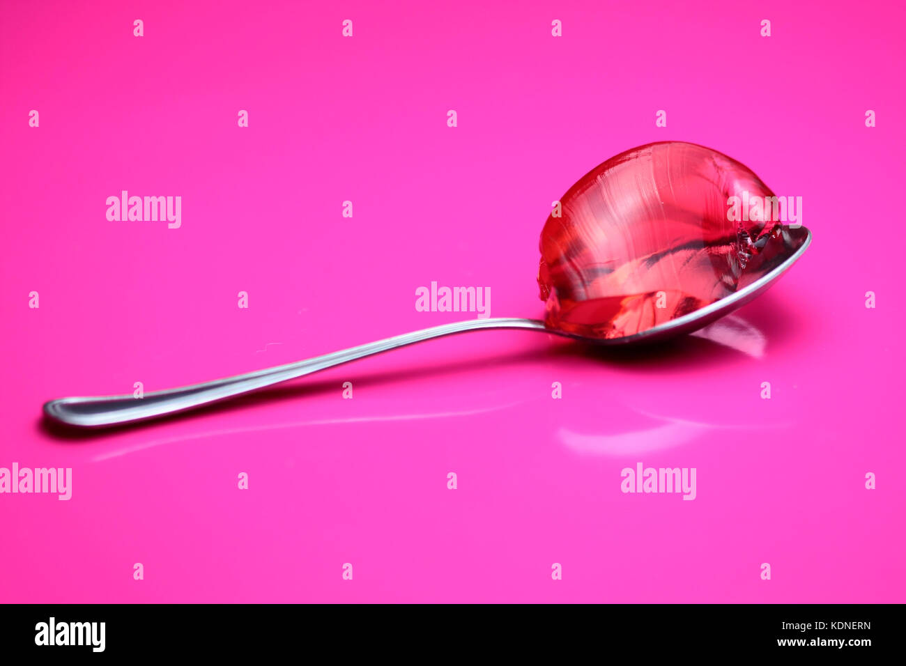 Red jelly on the tea spoon on the pink background Stock Photo - Alamy