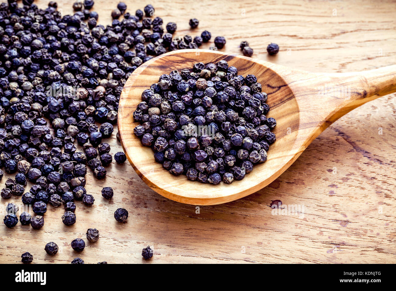 Closeup black pepper in wooden spoon on shabby teak wood table ...