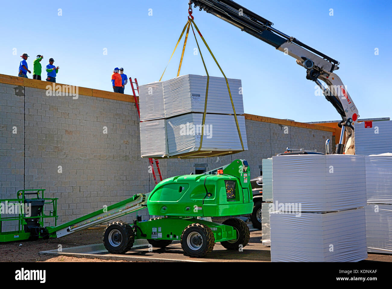 Mobile crane lifting polystryrene insulation tile pallets onto a roof ...