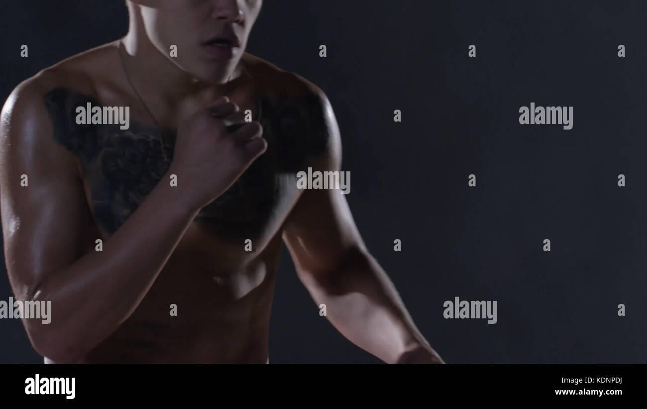 Man with tattoos boxing in a dark room with smoke. Aggressive shirtless ...