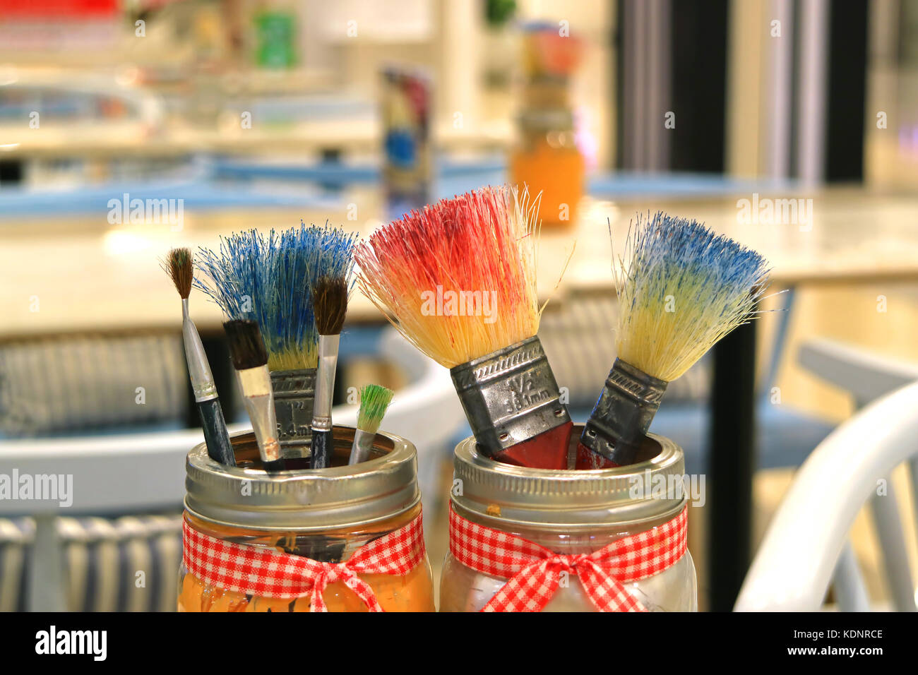 Many paint brushes in the jars with blurred painting classroom in ...