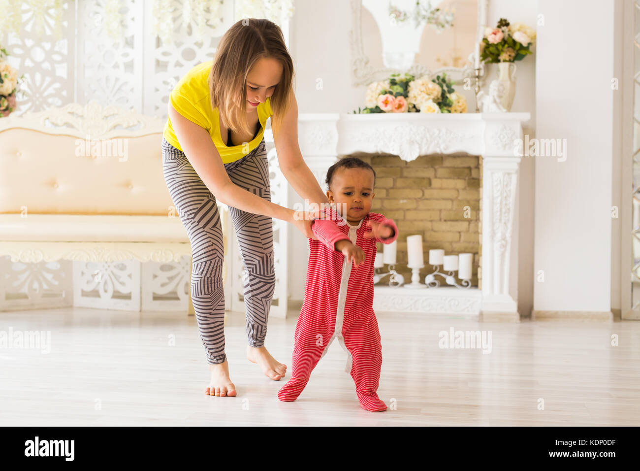 Cute little mixed race baby learning to walk, mom is holding his hands ...
