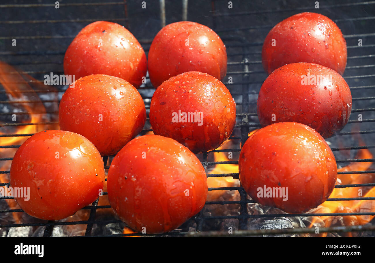 Red tomatoes cooked on fire barbecue grill with smoke and flame, close ...