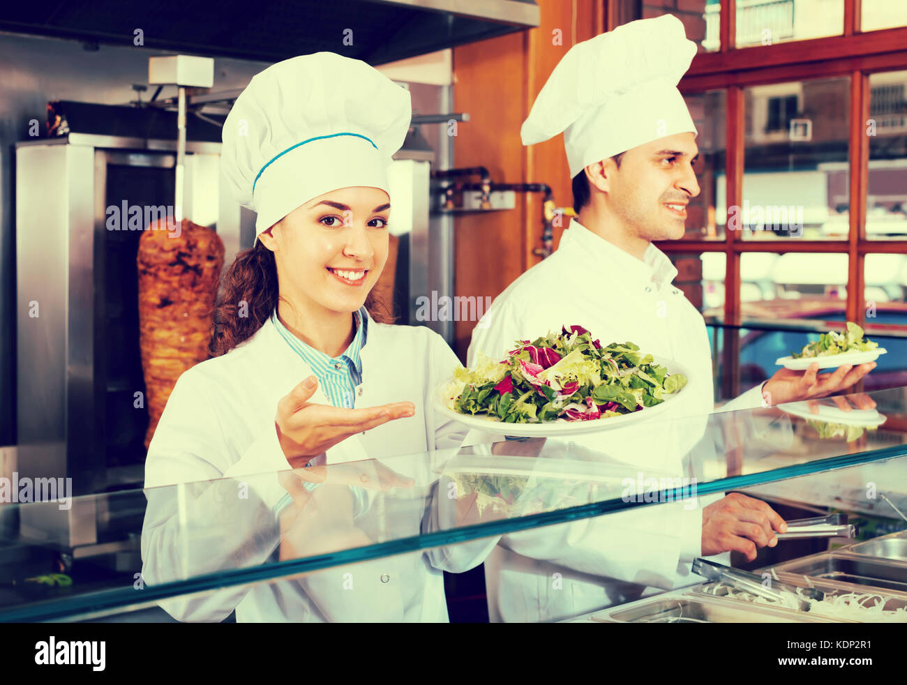 Two joyful smiling chefs offering kebab and vegetables salad at bistro ...