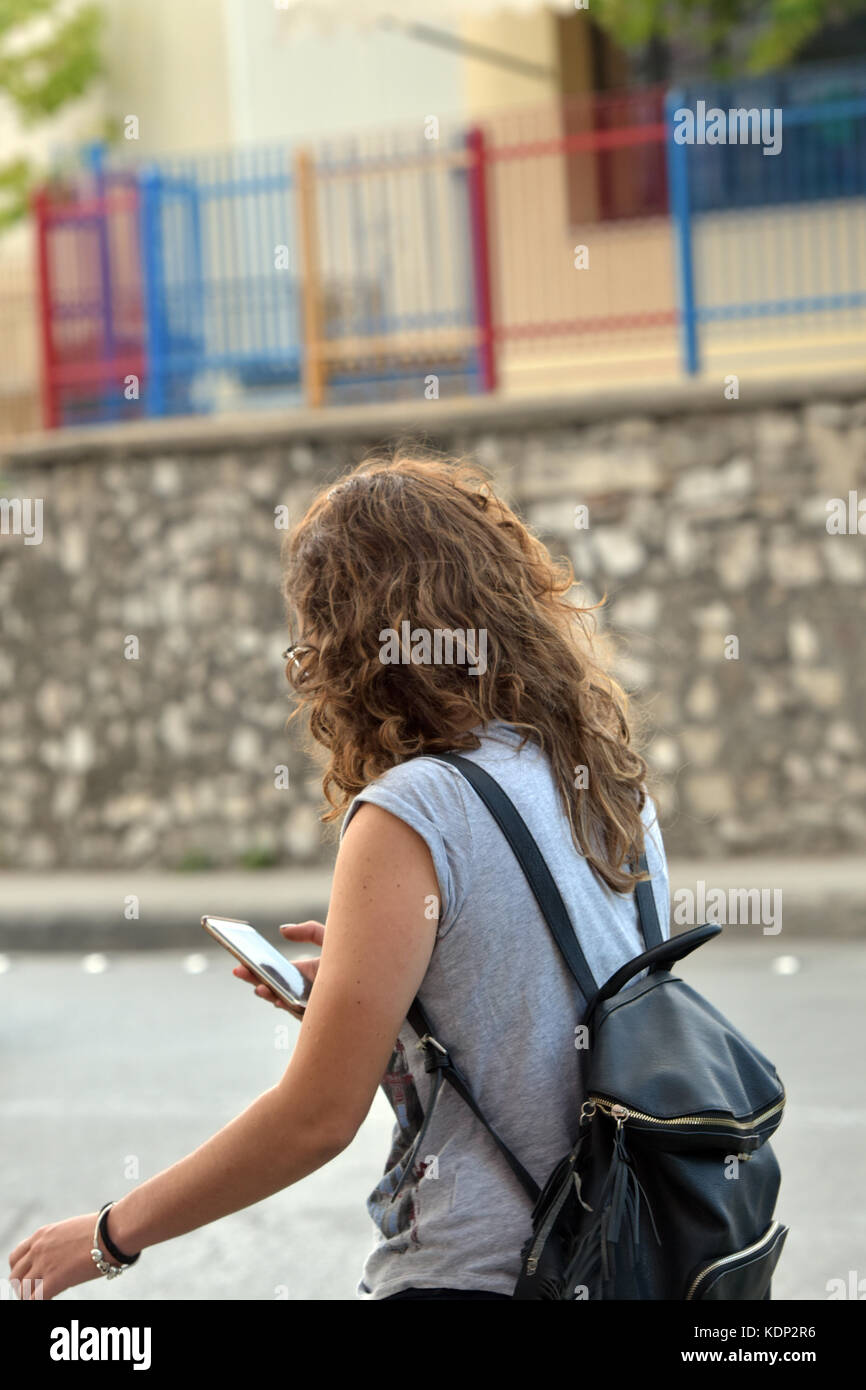a young woman walking along a street using a mobile phone or portable ...