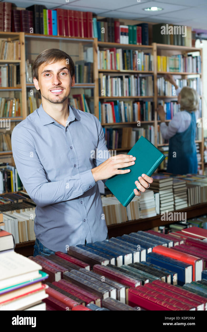 Young smiling man holding book in hard cover in book store Stock Photo ...