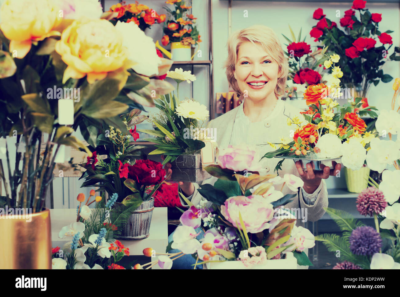 Adult cheerful female customer choosing flowers in floral department ...