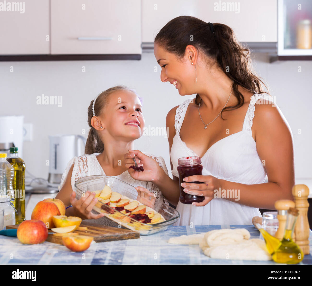 Portrait of smiling young woman and child cooking apple strudel indoors ...