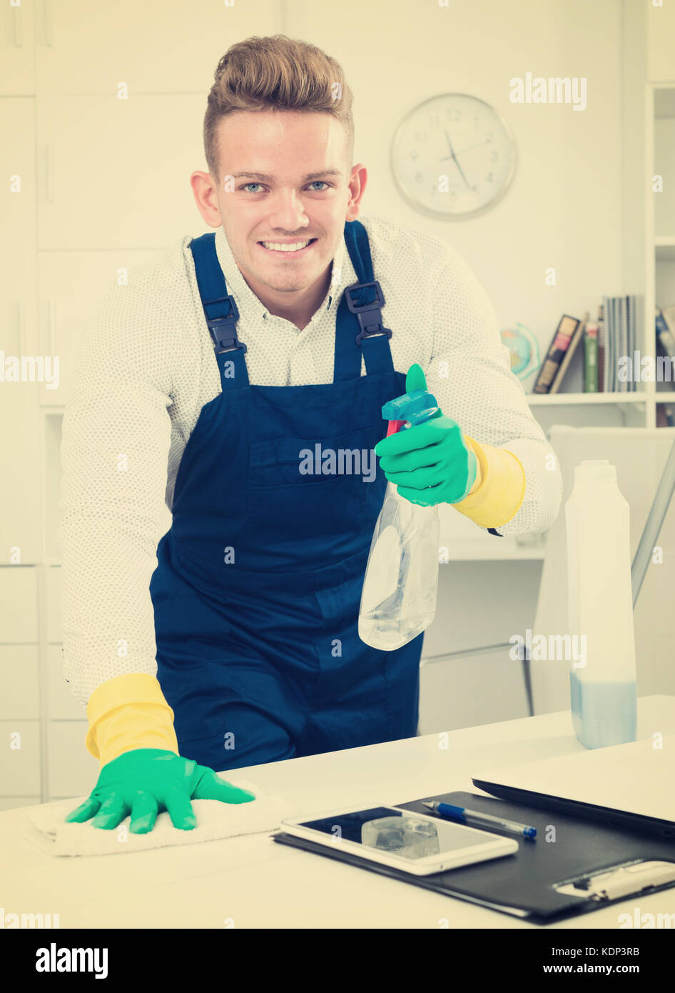 Young male janitor dusting office desk and smiling indoors Stock Photo ...