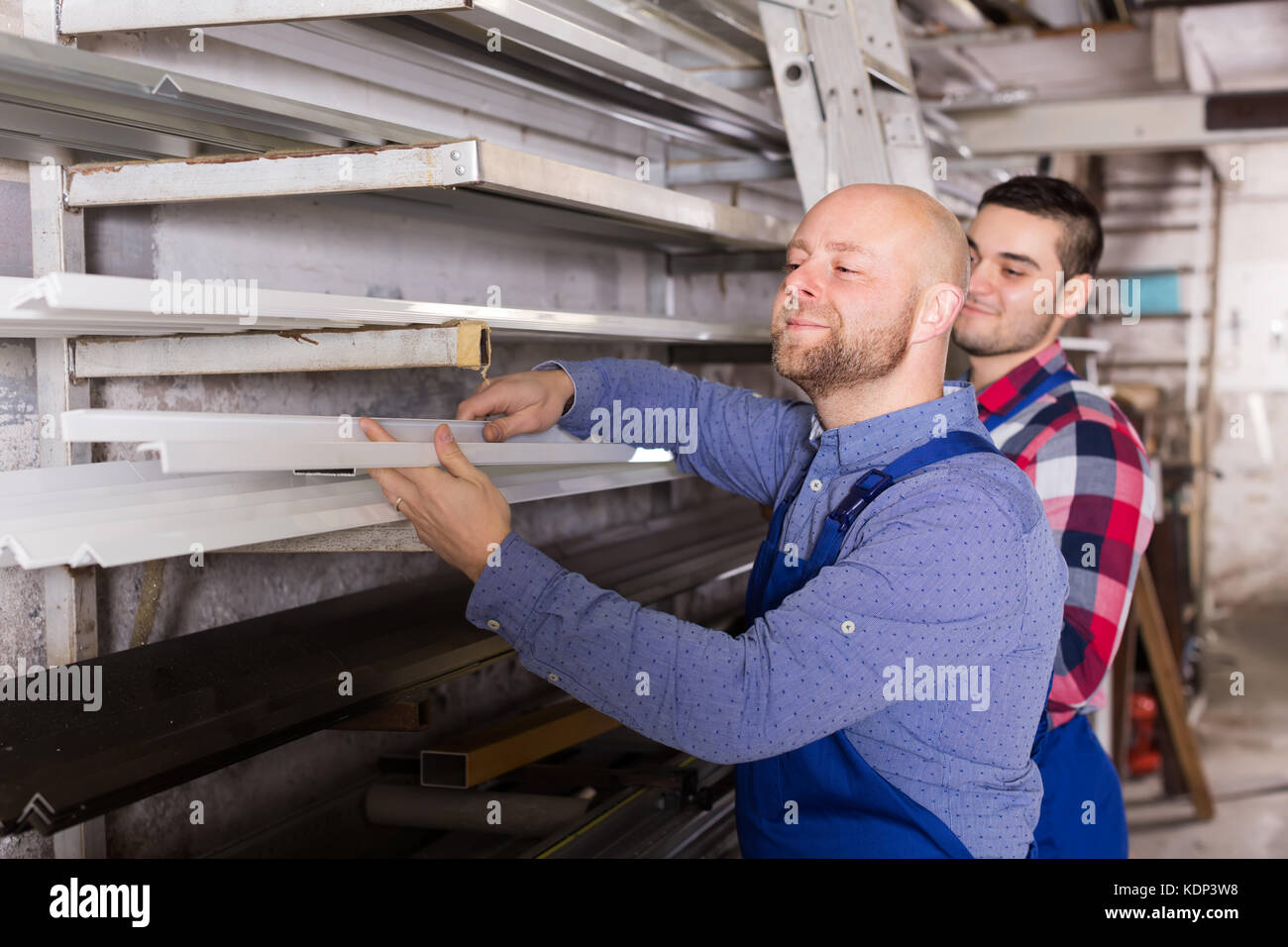 Two positive smiling workers in uniform choosing PVC window profile at ...