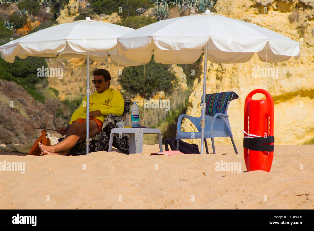A beach life guard under the shade of his sun brolly while scanning the ...