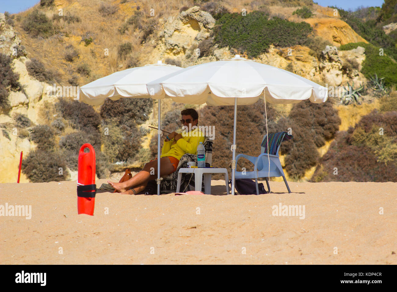 A beach life guard under the shade of his sun brolly while scanning the ...
