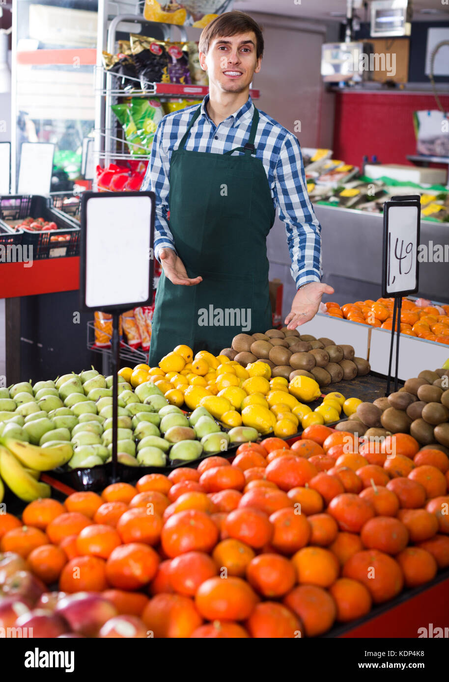 Portrait of young man offering ecological fruits in grocery and smiling ...