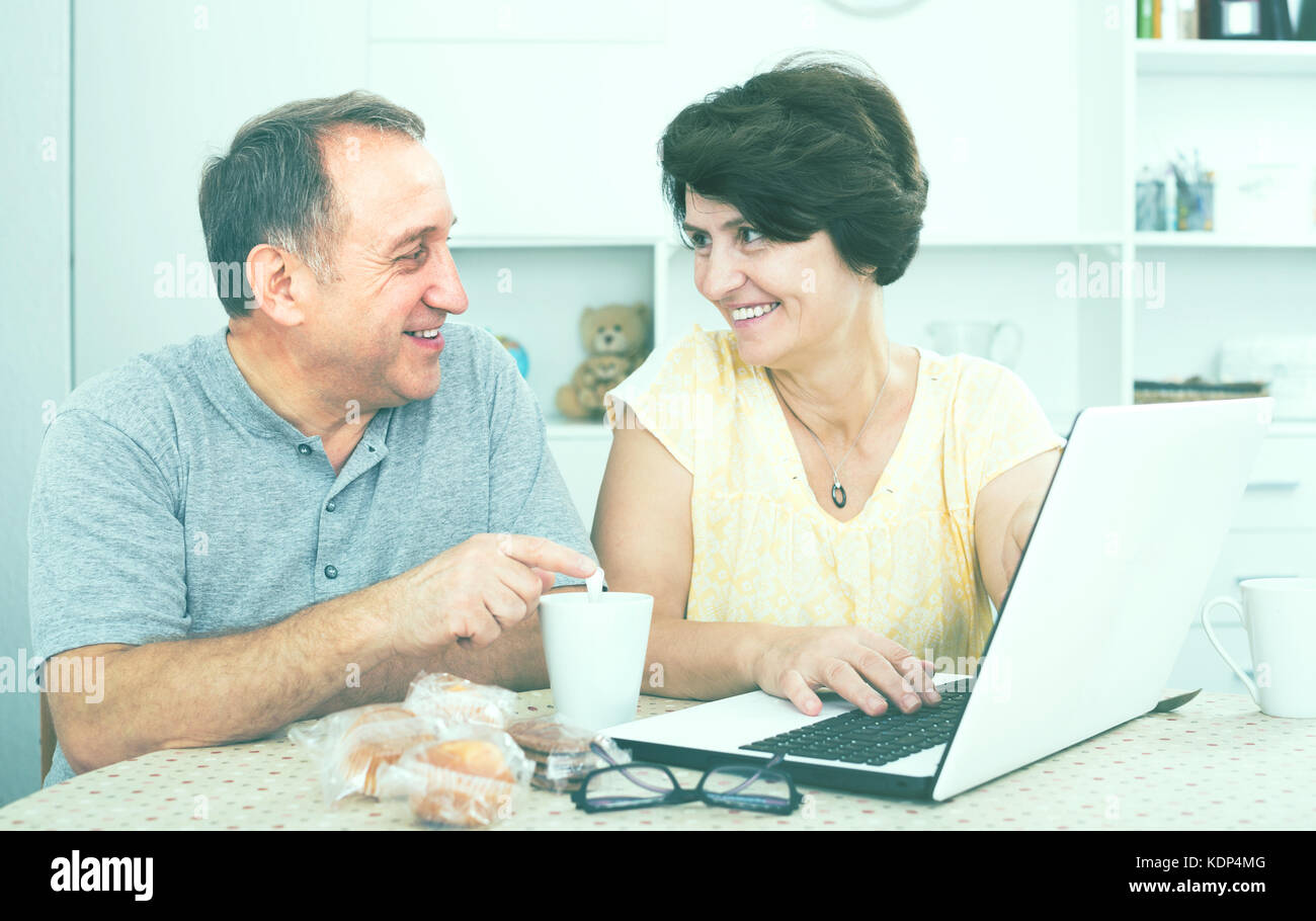 Smiling mature couple looking documents on laptop indoors at home ...