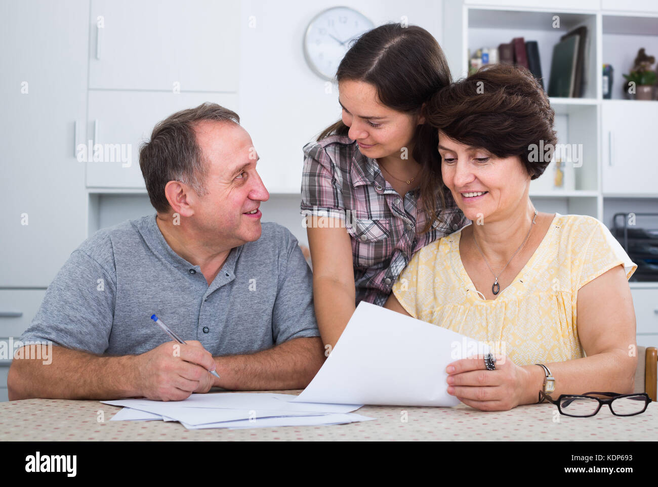 Senior man and woman signing documents with help of young woman indoors ...